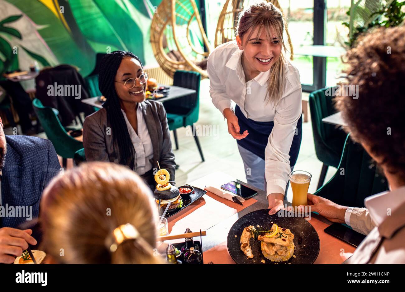 Smiling waitress serving meal to group of business people in restaurant ...