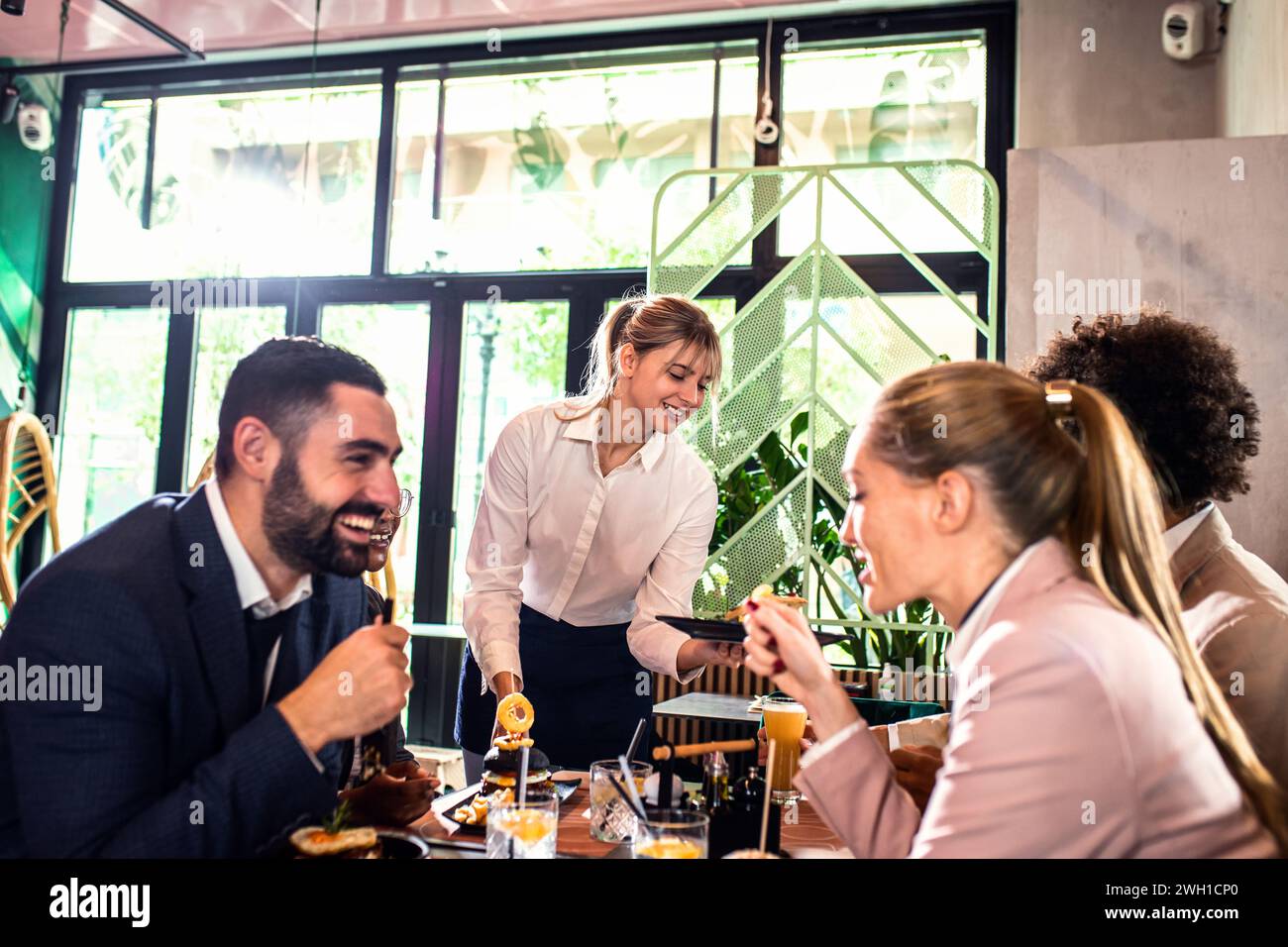 Smiling waitress serving meal to group of business people in restaurant ...