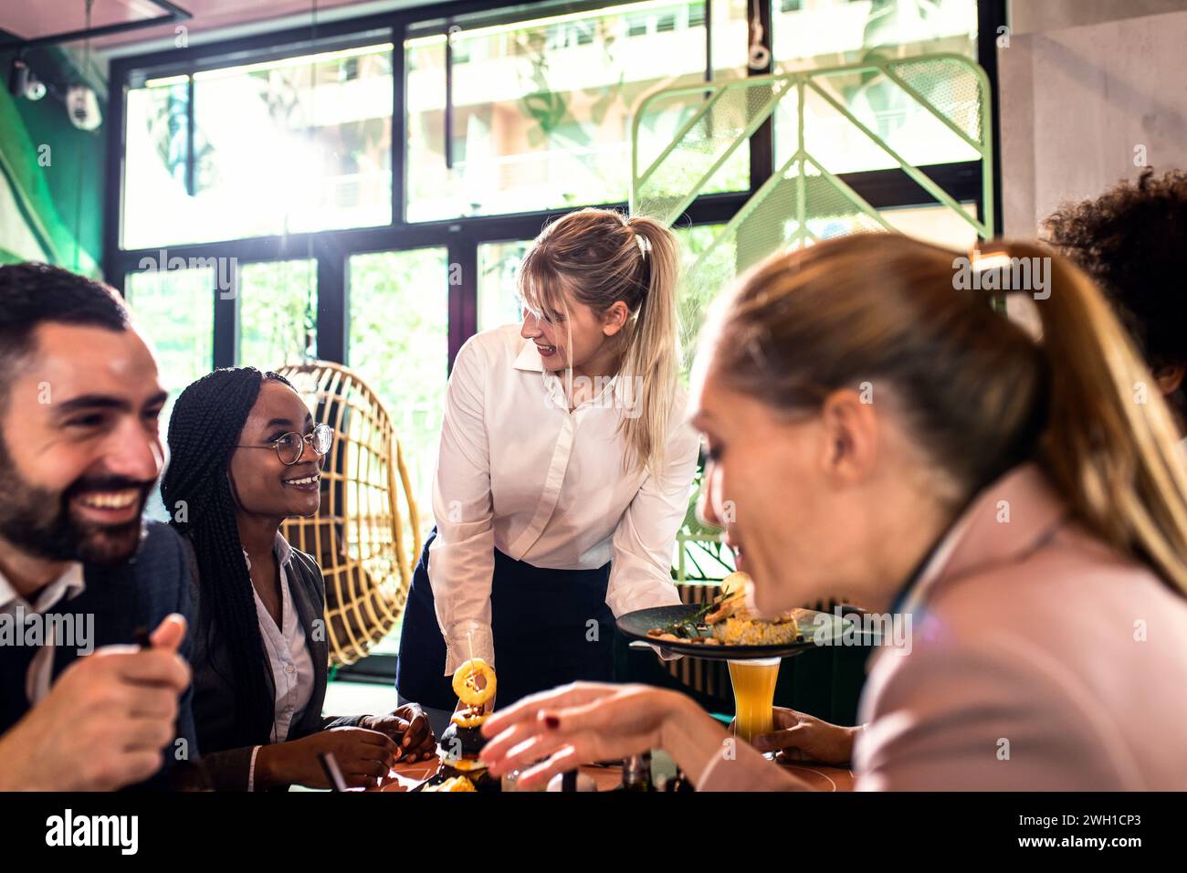 Smiling waitress serving meal to group of business people in restaurant ...