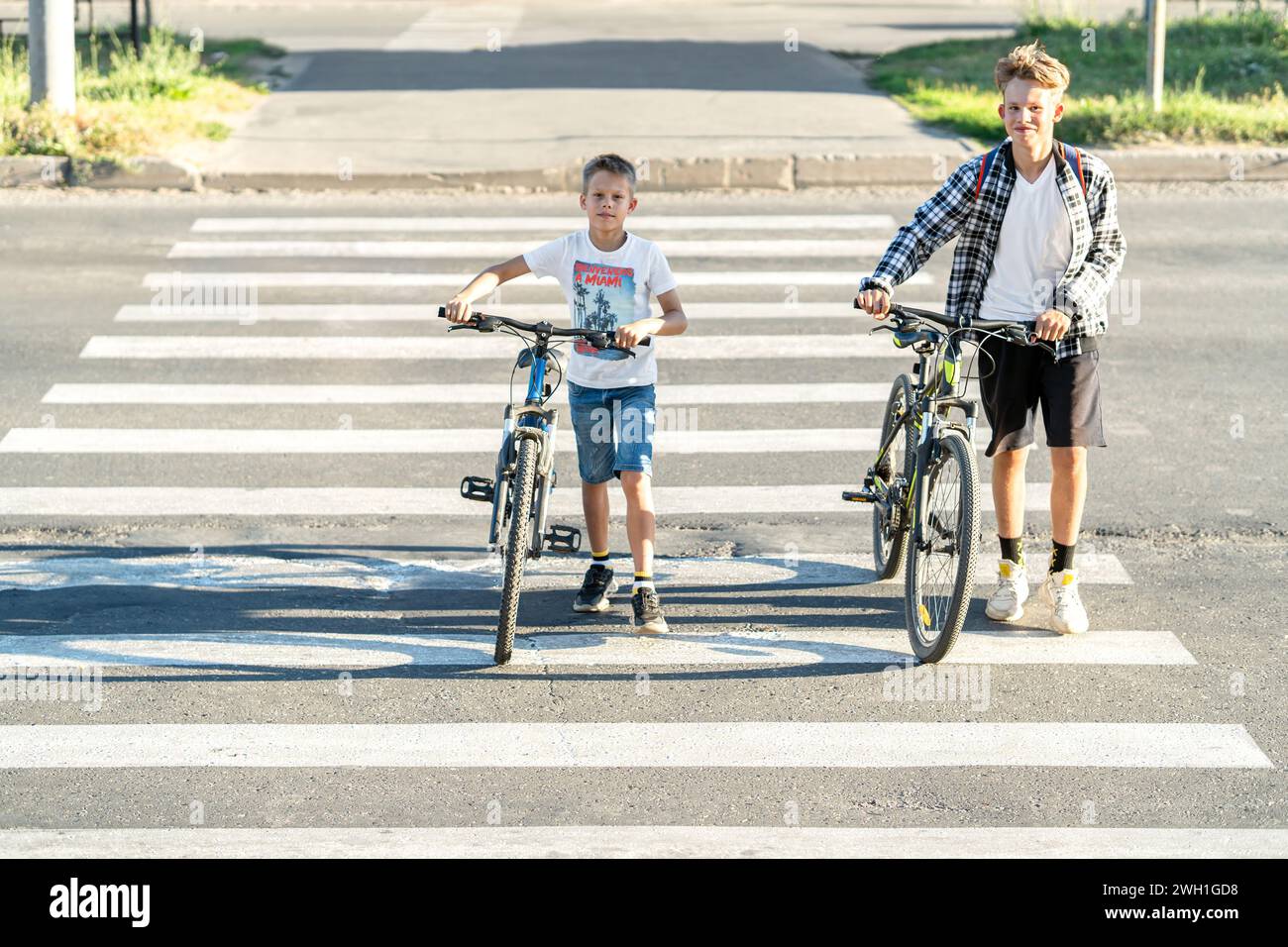 Two boys in everyday attire walking and wheeling bicycles through a ...