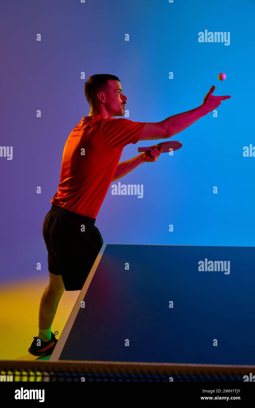 Side view. Young athlete man serving ball in table tennis keeping eyes ...