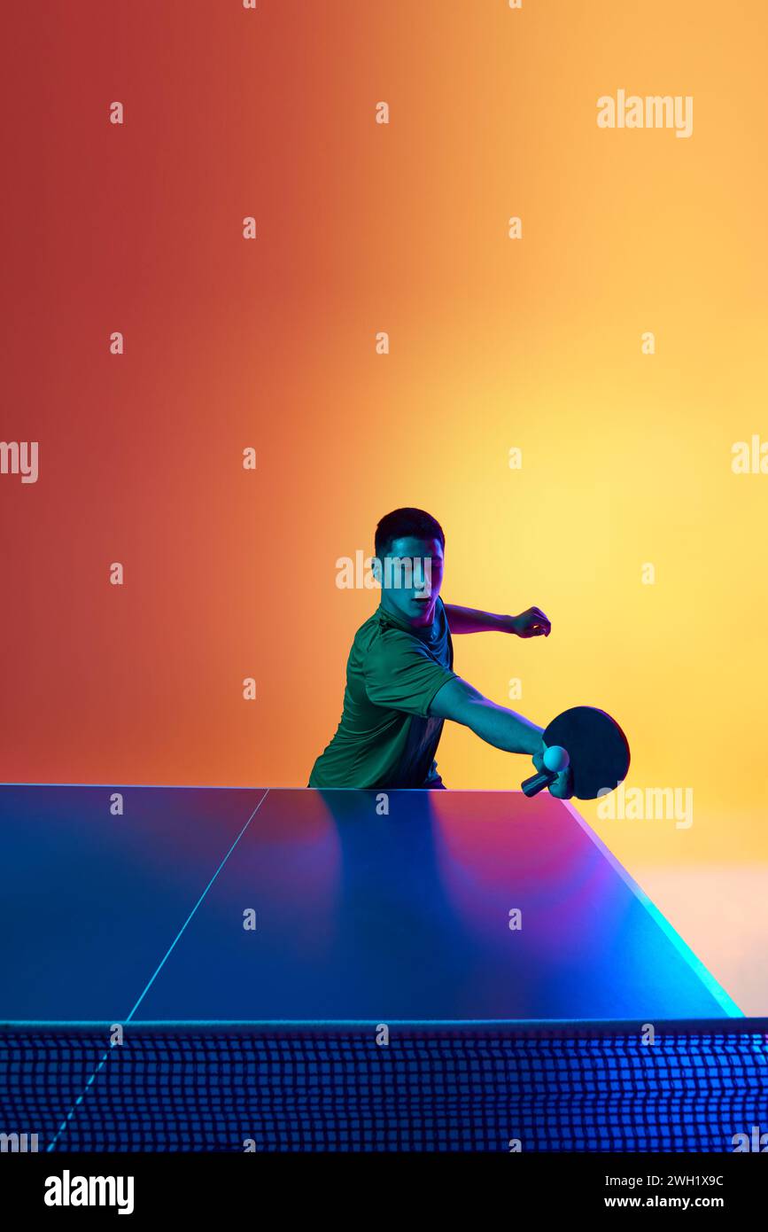 Athletic Asian man playing ping pong in neon light against warm yellow ...
