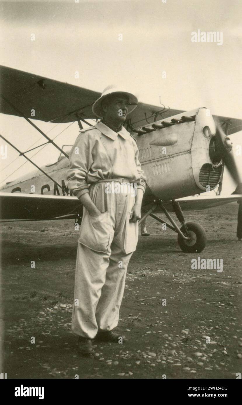Man in jumpsuit and explorer hat next to a single engine biplane ...
