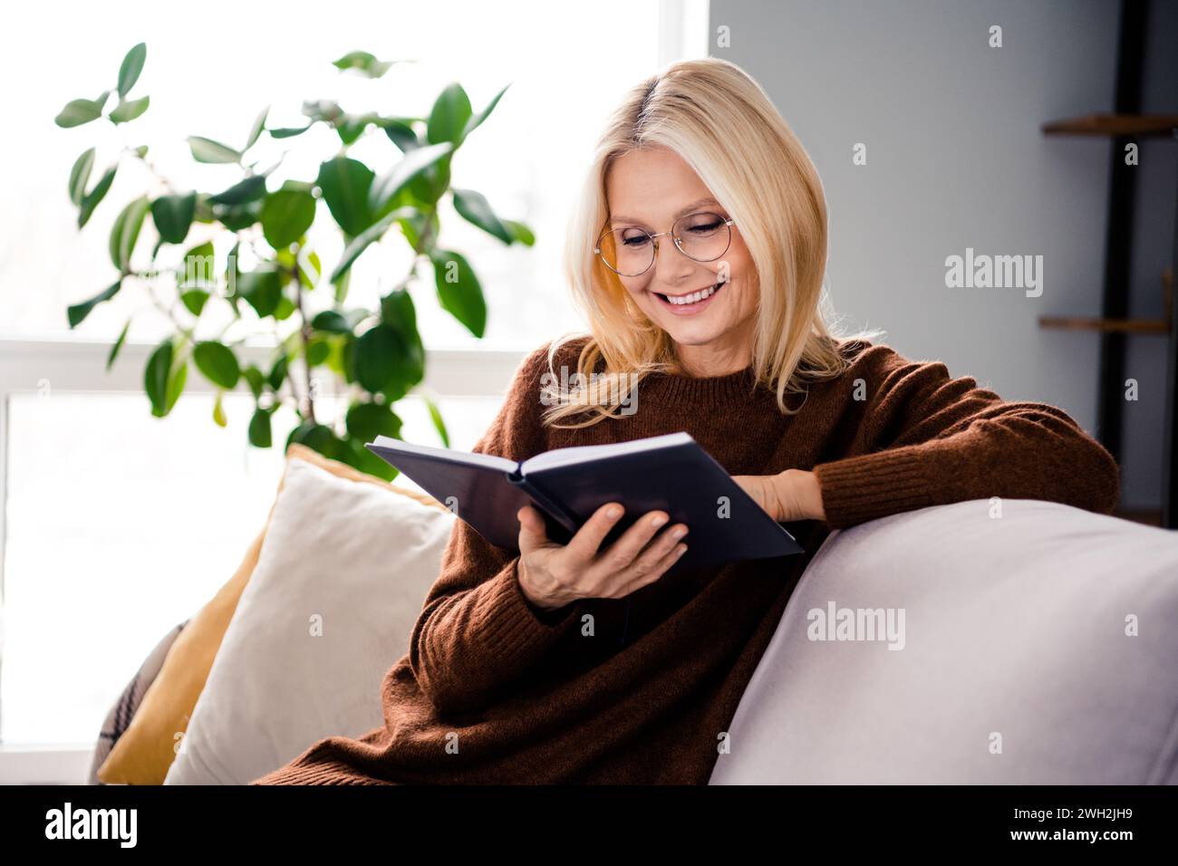 Photo of cheerful lovely cute woman pensioner sitting on couch reading ...