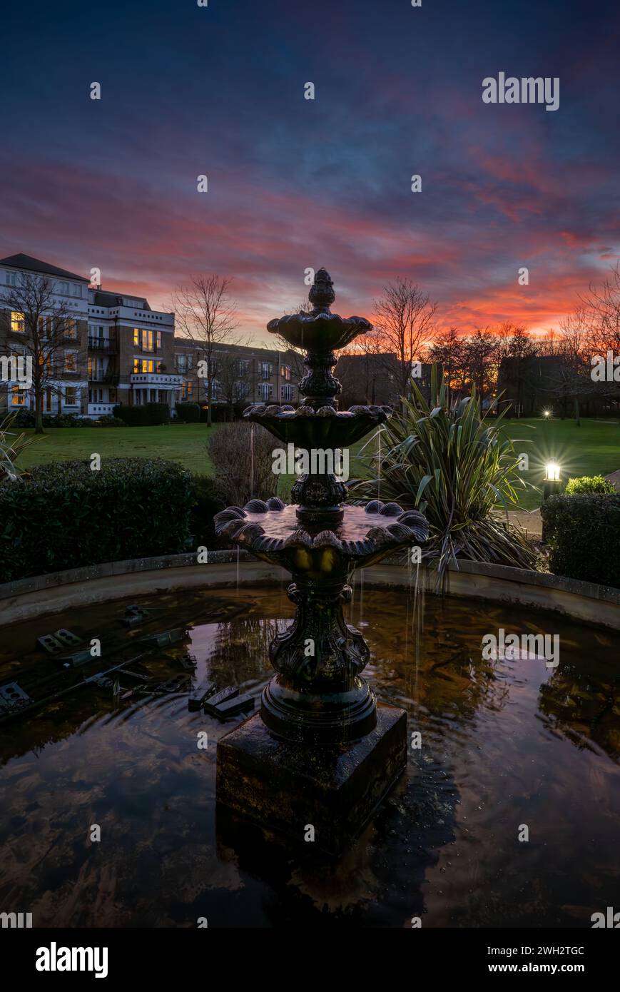 Fountain and pond in a park at sunset with a pink sky. Dusk view in ...