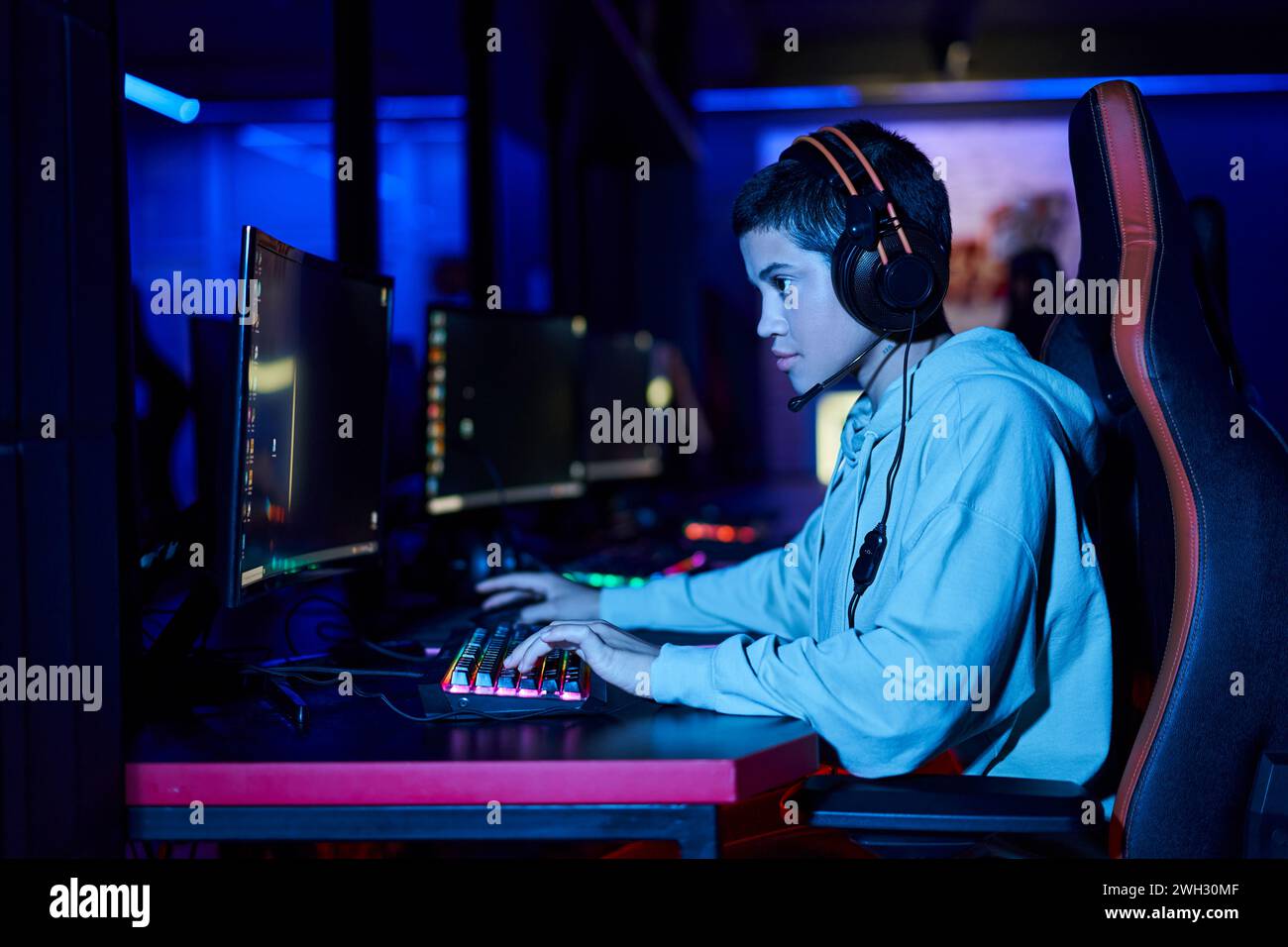 focus on concentrated young woman playing game in a blue lit room ...