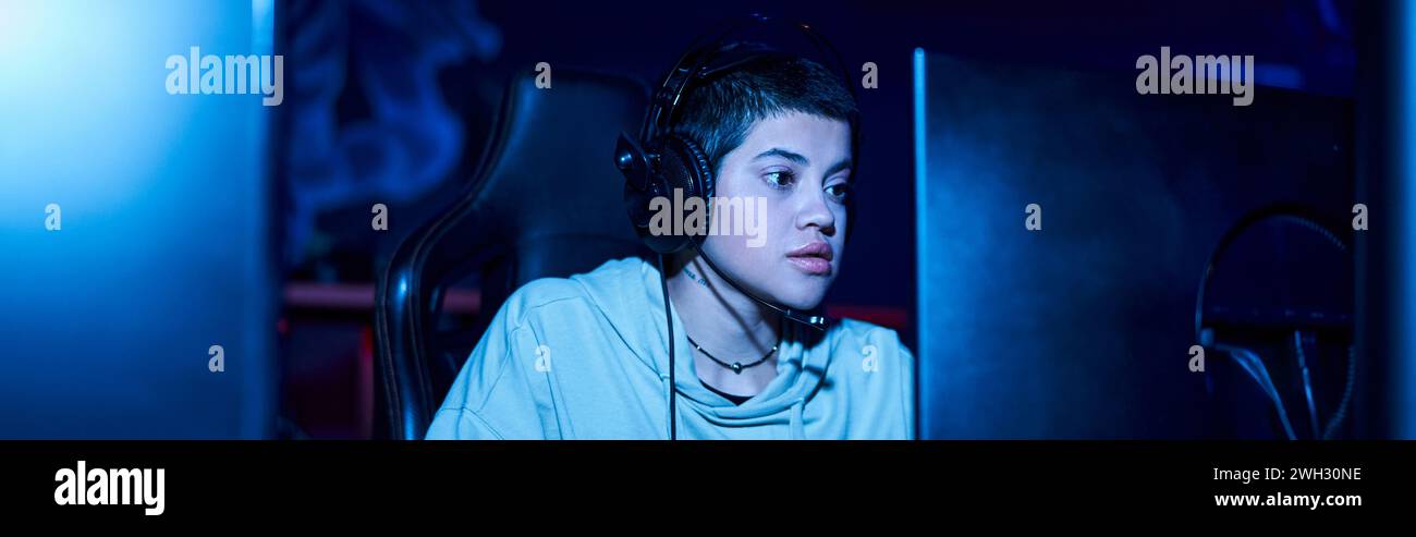 focused gamer looking at computer monitor while playing game in a blue ...