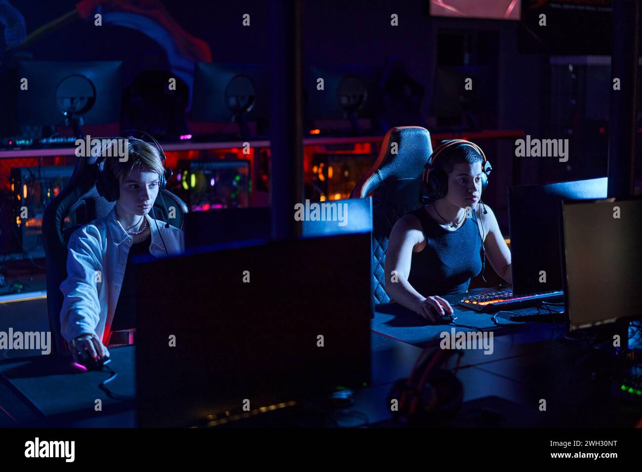 focused gamers in headphones looking at monitors while playing ...