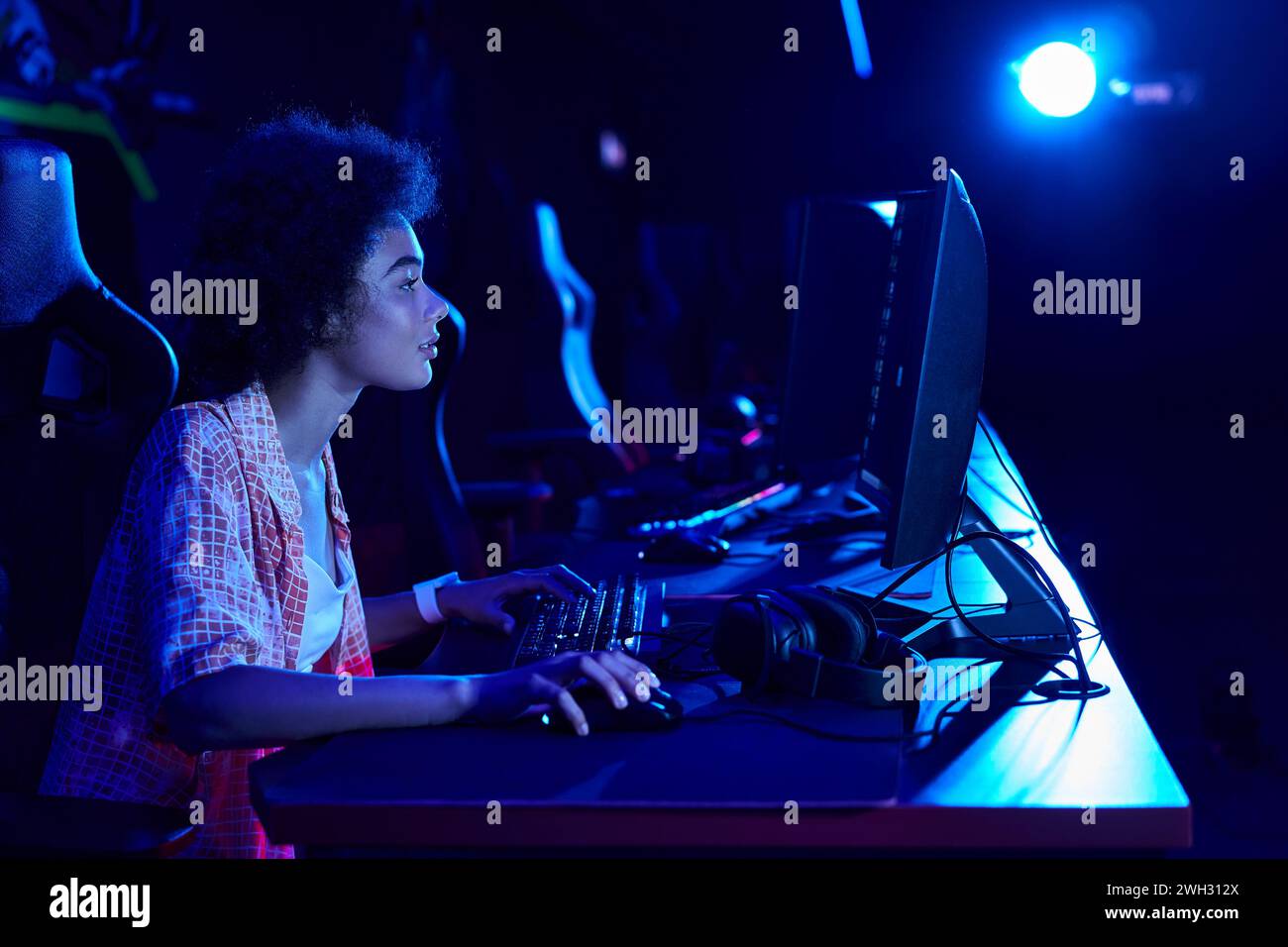 side view of focused african american woman gaming intensely in a blue ...
