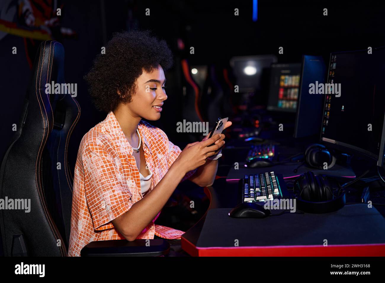 happy black woman sits near computer, her face illuminated by the blue ...