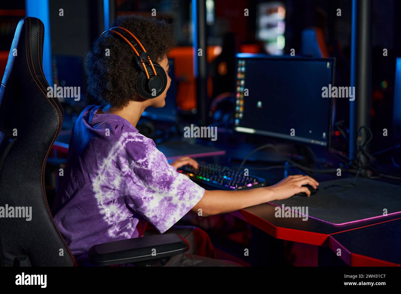 curly african american gamer in headphones playing computer game while ...