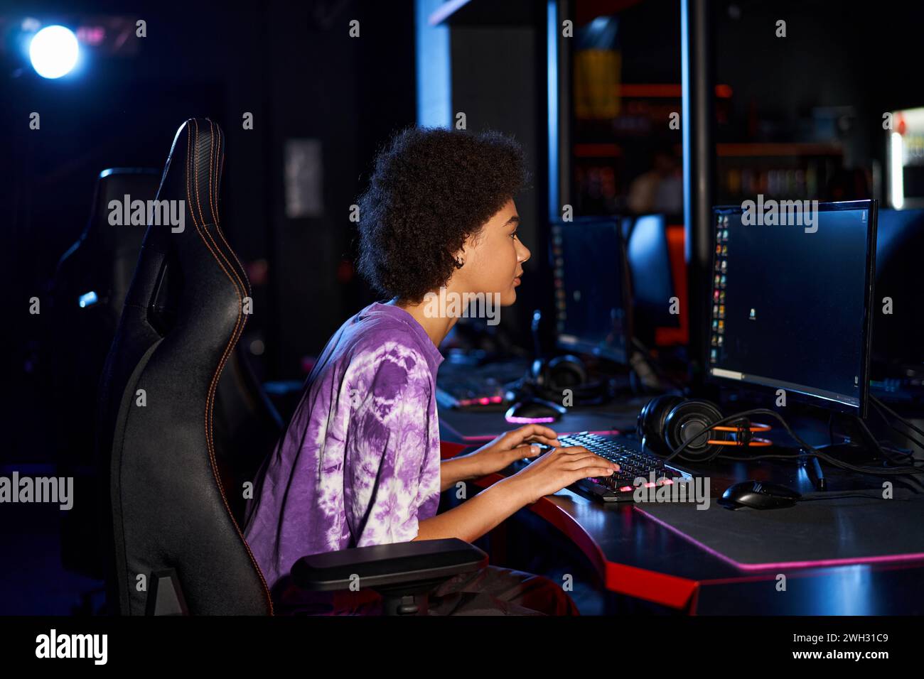 curly african american gamer in headphones playing computer game while ...