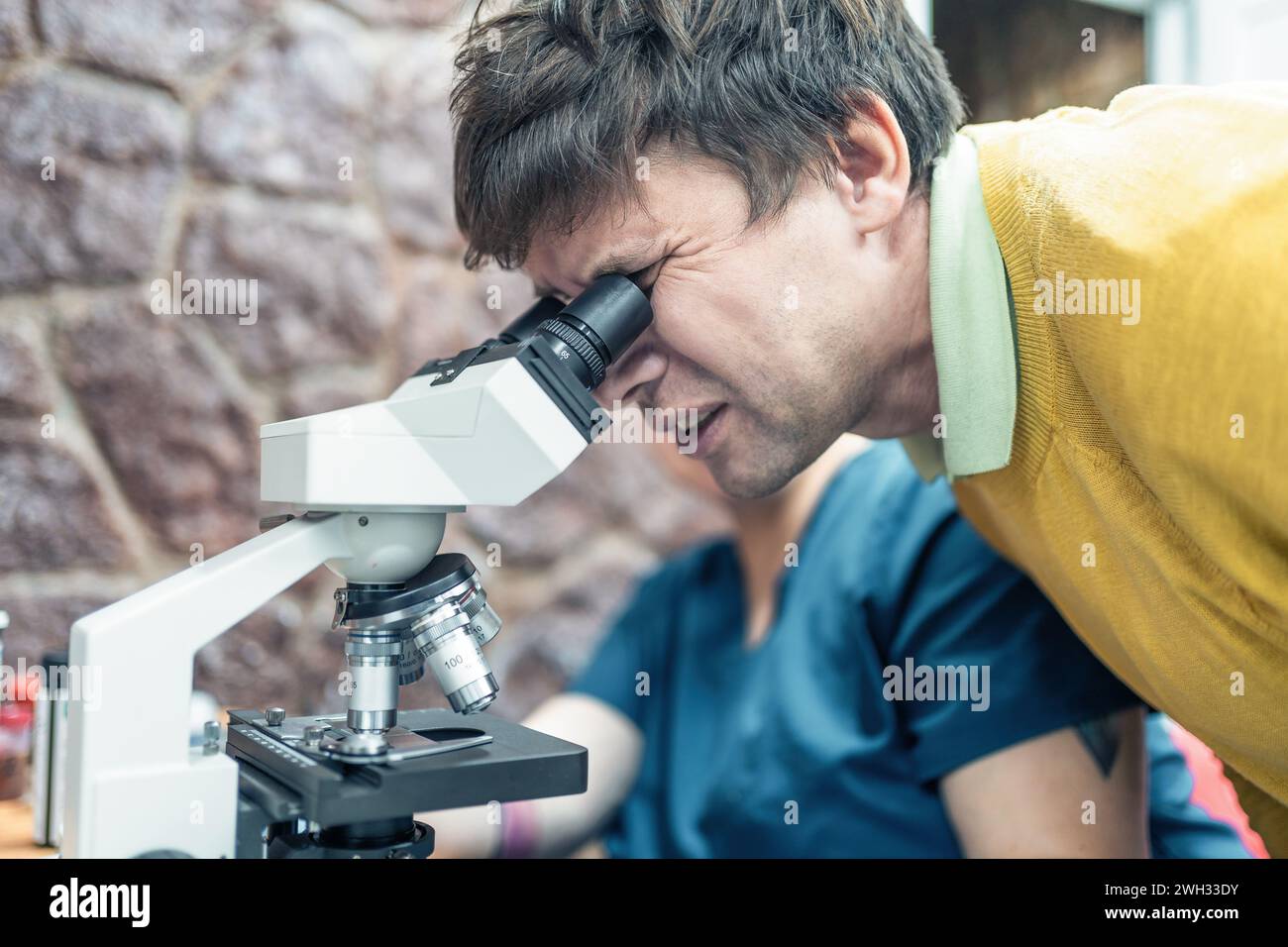 Man student or scientist examines specimen under microscope, observing ...