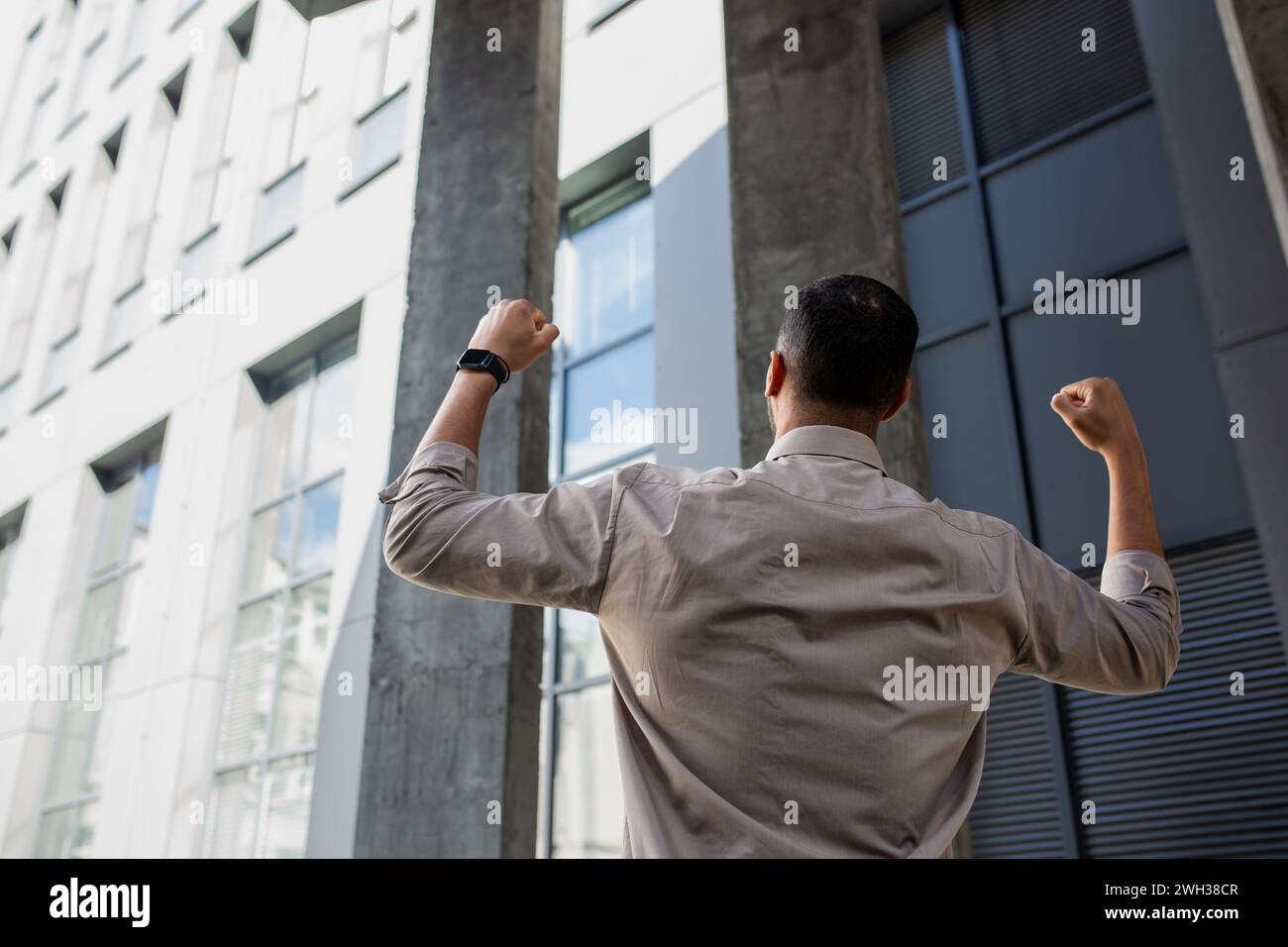Back view of brunet man in shirt making power sign with clenched fists ...