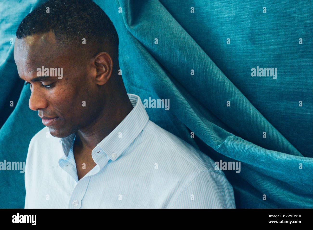 A man is seen standing upright in front of a vibrant blue curtain ...