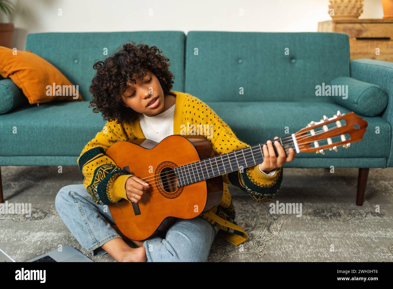 African American woman learning guitar watching tutorial on laptop at ...