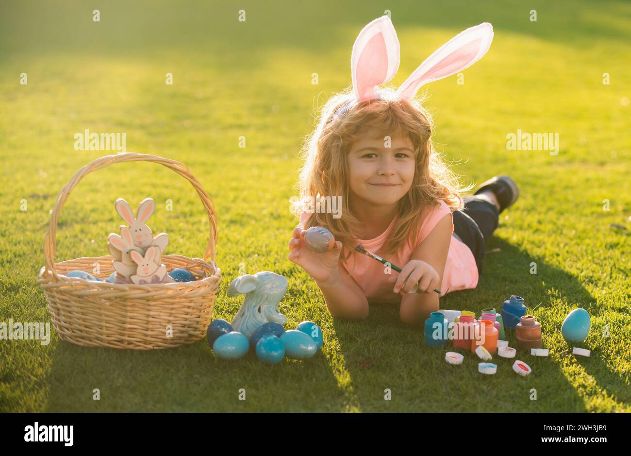 Child boy with easter eggs and bunny ears laying on grass. Funny boy ...