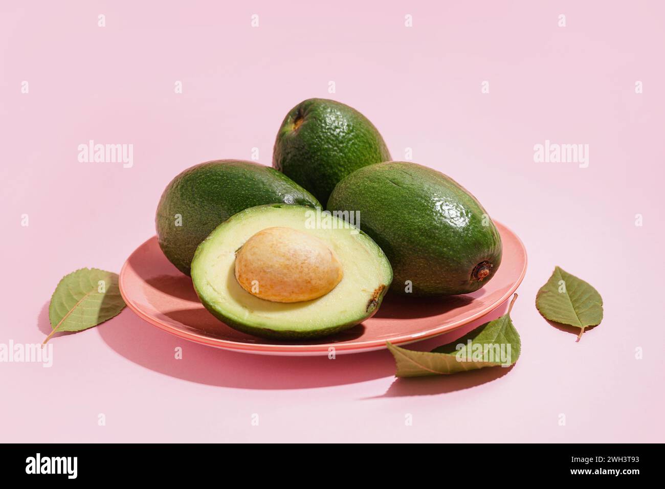 Plate with fresh ripe avocados and leaves on pink background Stock ...