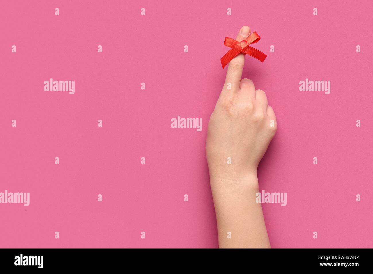 Female hand with red bow on index finger against pink background ...