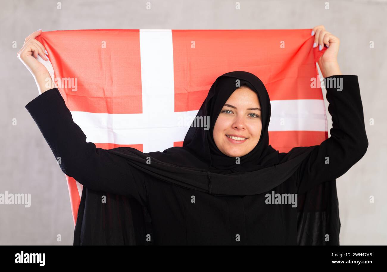 Balanced smiling Muslim woman in traditional black hijab holds flag of ...