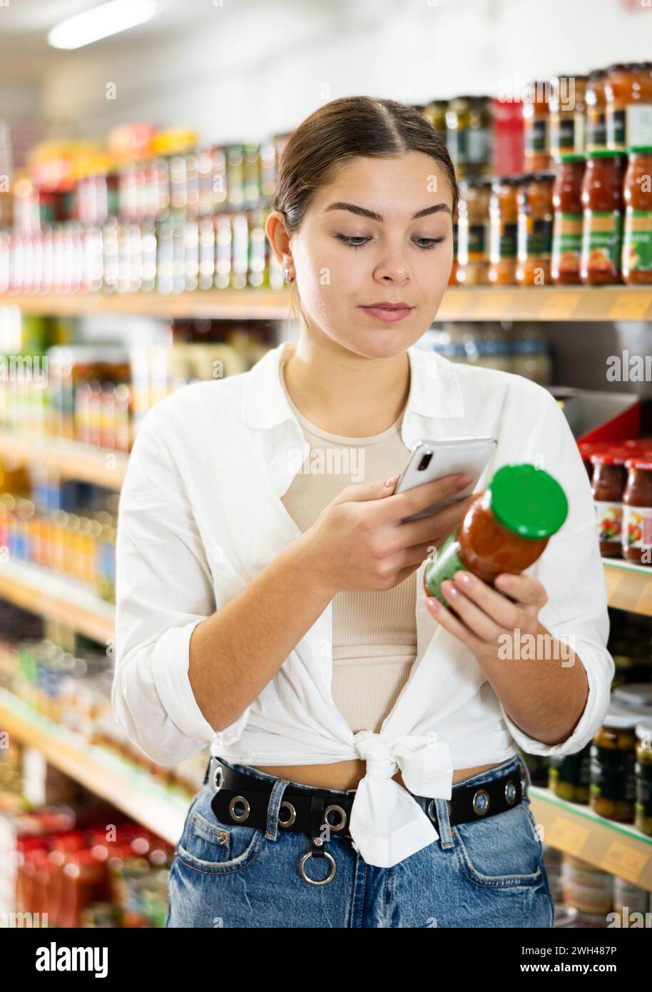 Young woman choosing preserved vegetables for herself in supermarket ...