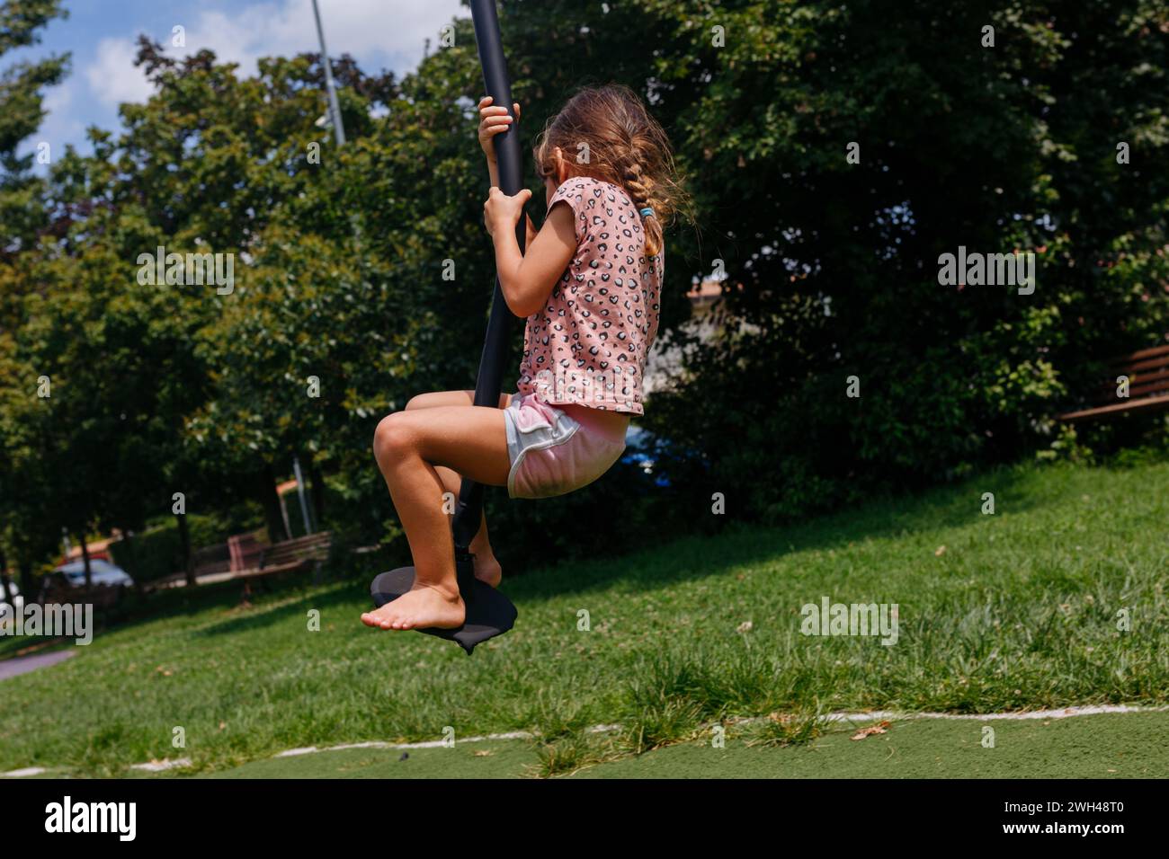 rear view of small girl having fun sitting on a pulley on a sunny day ...