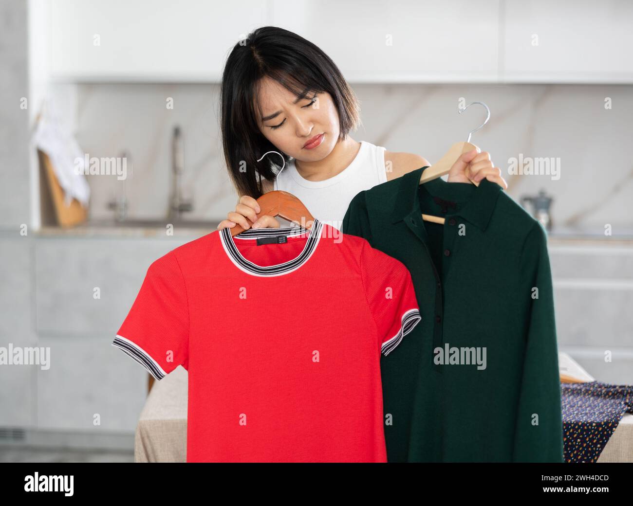 Sad young Asian girl trying to choose a dress in the kitchen Stock ...