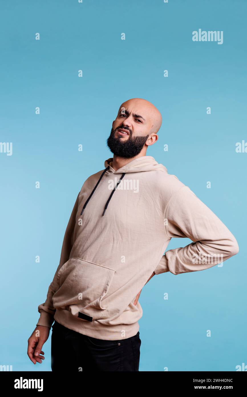 Arab man grimacing in pain while holding lower back and looking at ...