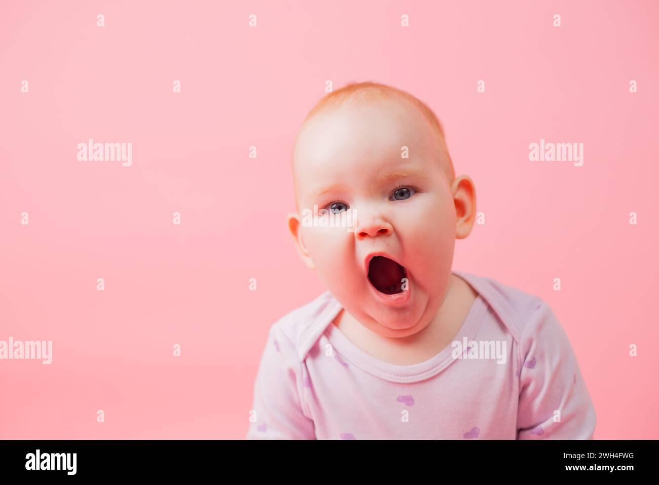 Portrait of a cute little yawning girl isolated on a pink background. A ...