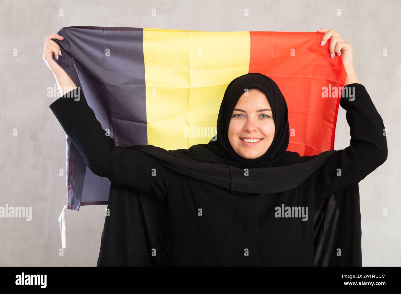 smiling Muslim woman in traditional black hijab holds flag of Belgium ...