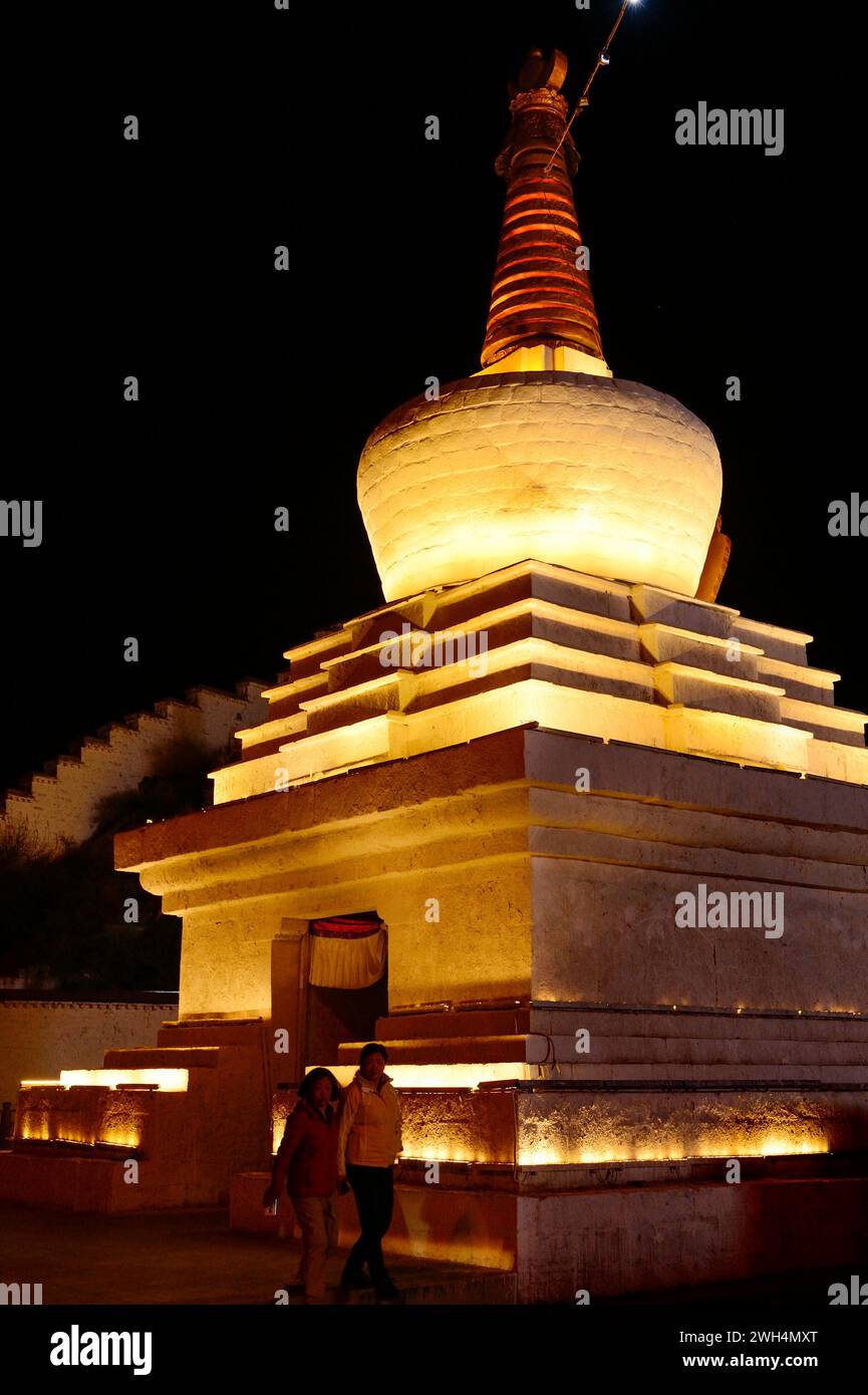 A couple holding hands stroll by an illuminated stupa, also known as a ...