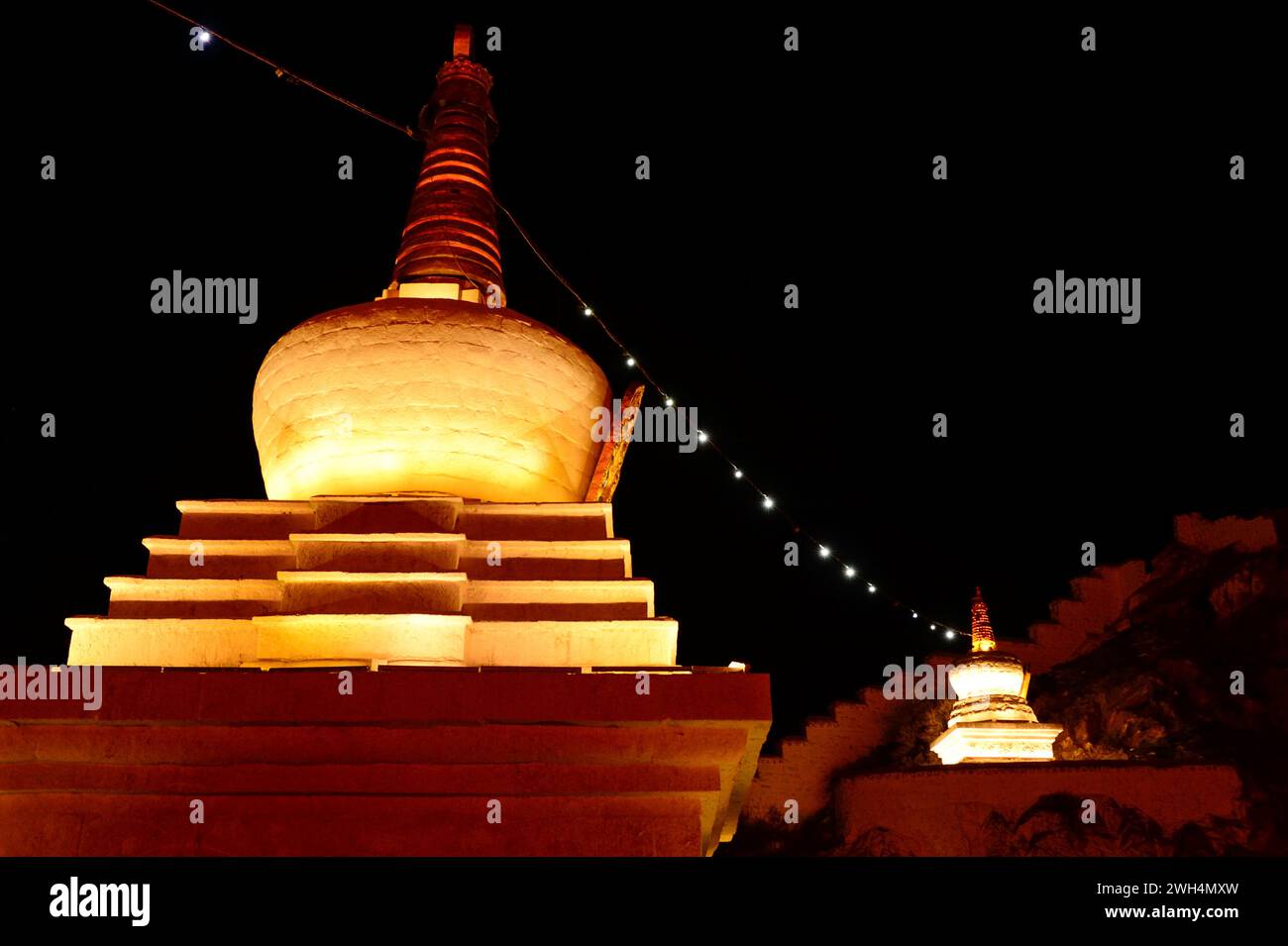 An illuminated stupa, also known as a chorten, lights up the night sky ...