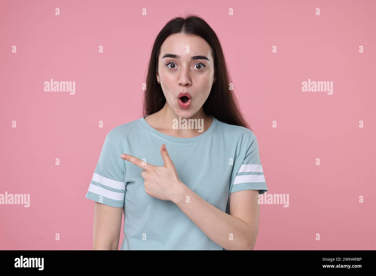 Portrait of surprised woman pointing at something on pink background ...