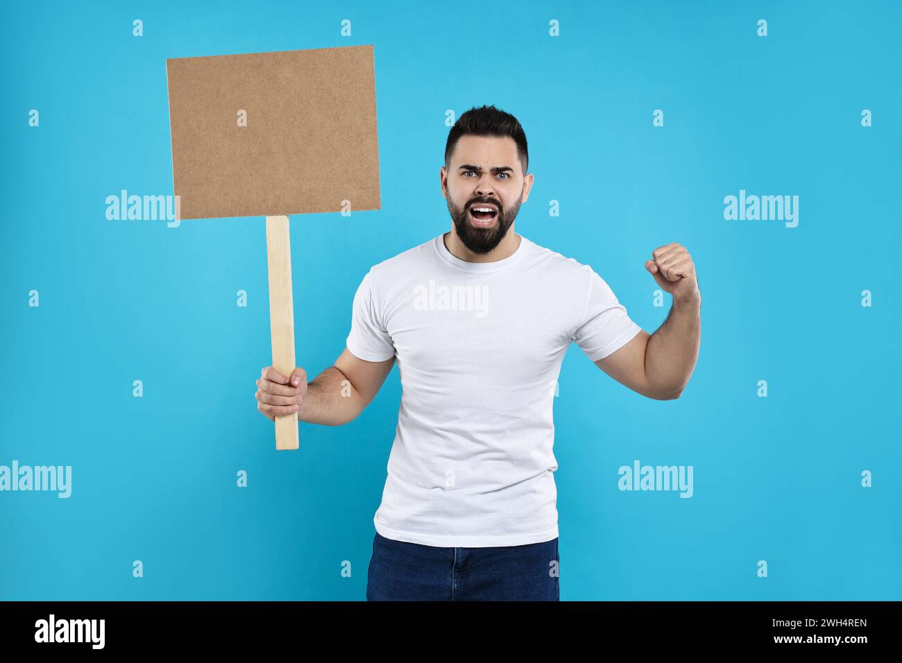 Angry man holding blank sign on light blue background, space for text ...