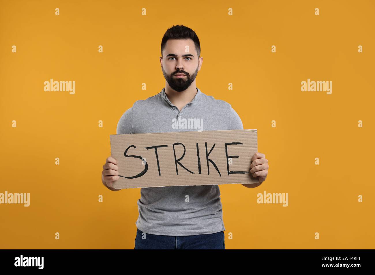 Man holding cardboard banner with word Strike on orange background ...
