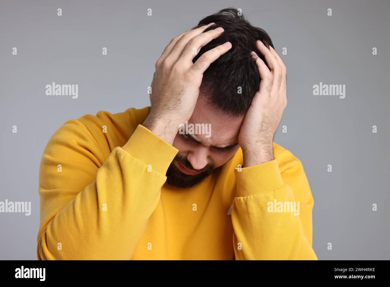 Sad man grabbing his head on light grey background Stock Photo - Alamy