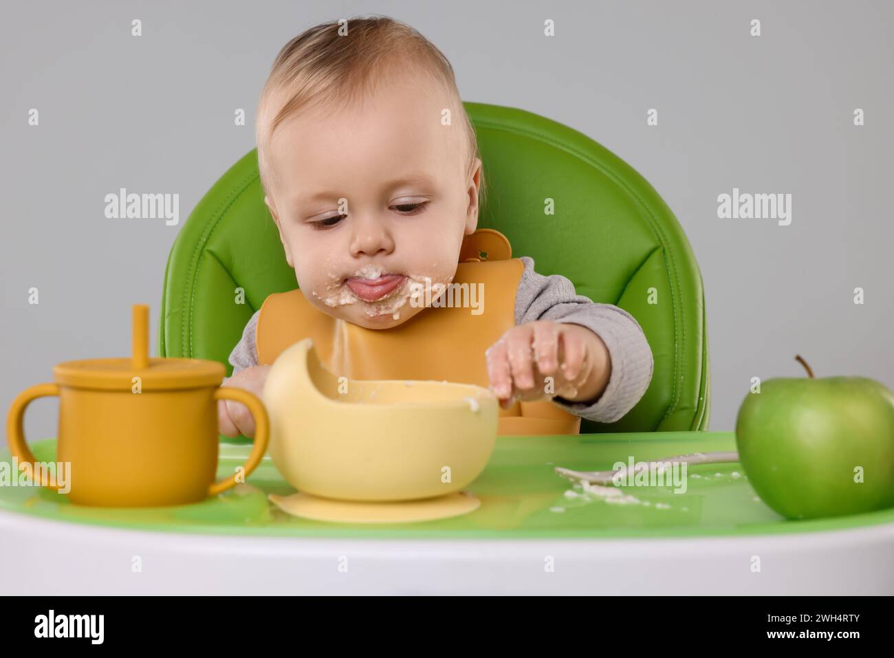 Cute little baby eating healthy food in high chair on gray background ...