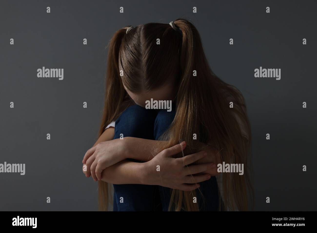 Sad girl sitting near dark grey background Stock Photo - Alamy