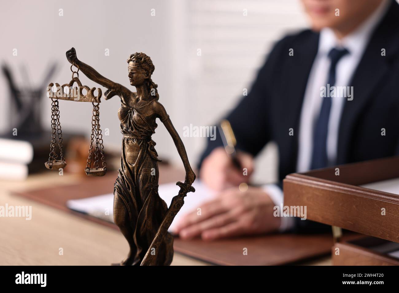 Notary writing notes at wooden table in office, focus on statue of Lady ...