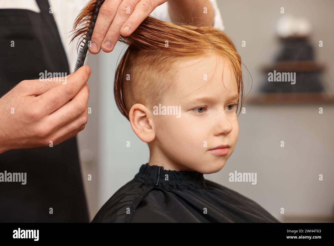 Professional hairdresser combing boy's hair in beauty salon, closeup ...