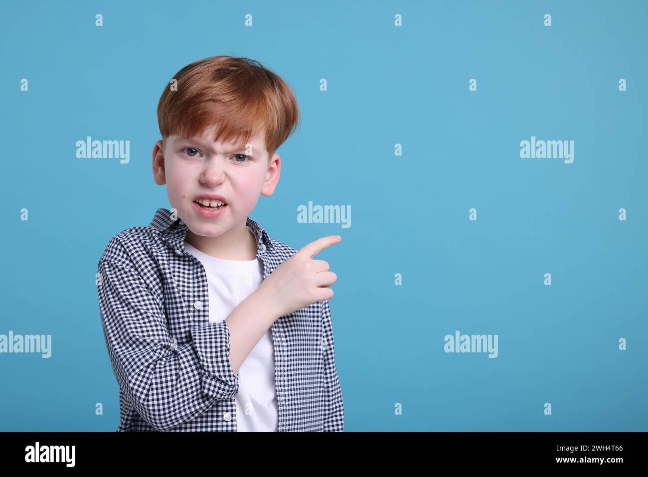 Surprised little boy pointing at something on light blue background ...