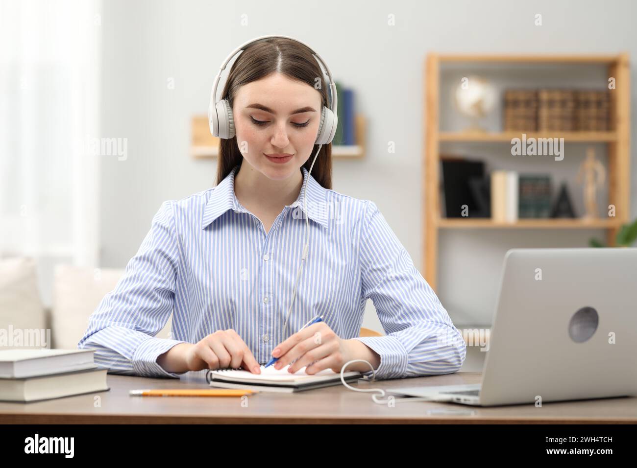 E-learning. woman taking notes during online lesson at table indoors ...