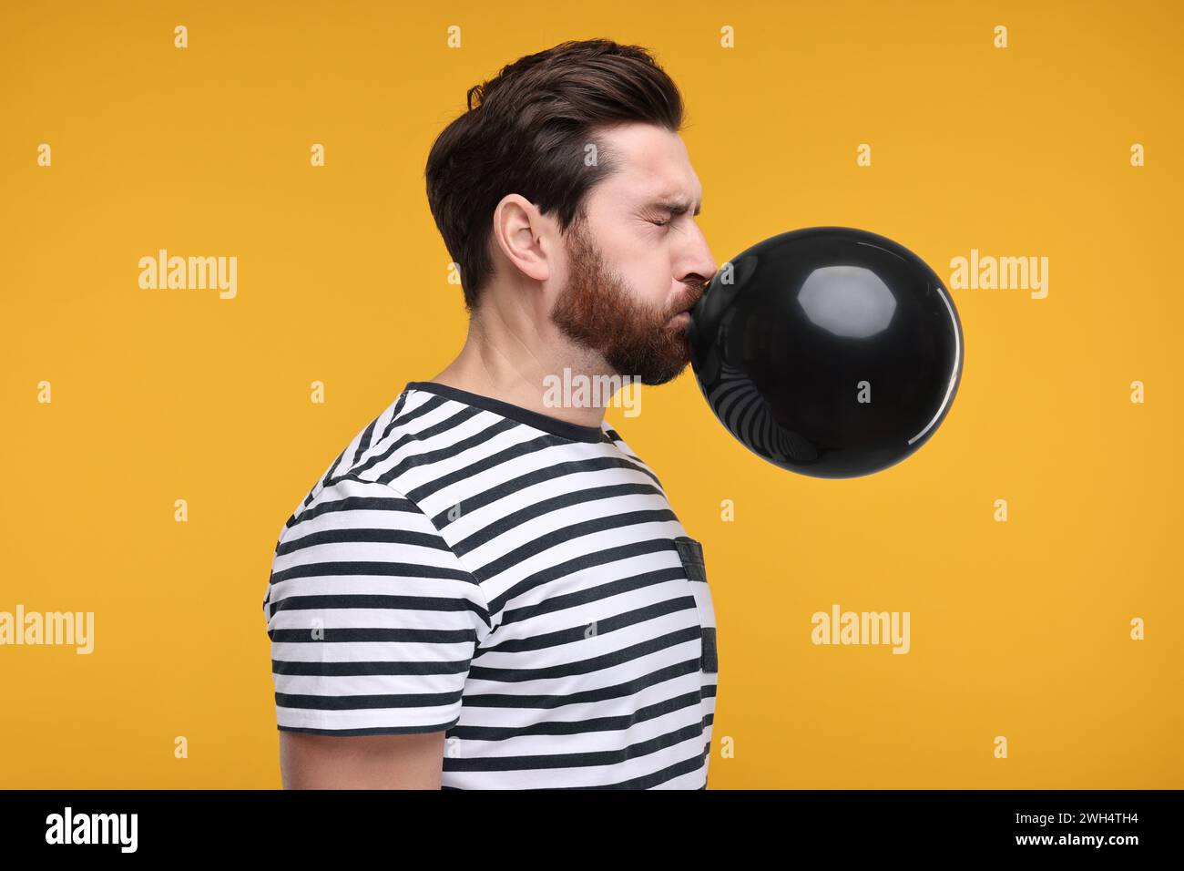 Man inflating black balloon on yellow background Stock Photo - Alamy