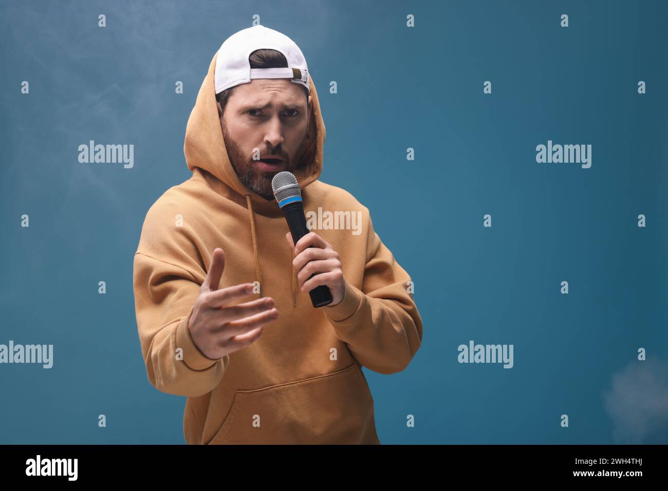 Singer in hoodie with microphone rapping on light blue background ...