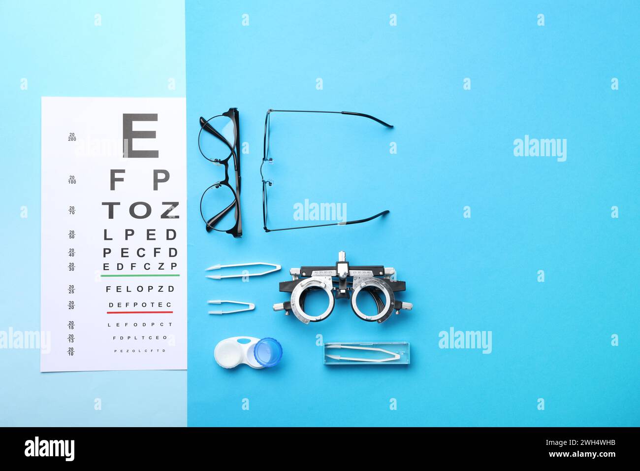 Flat lay composition with vision test chart and glasses on light blue ...