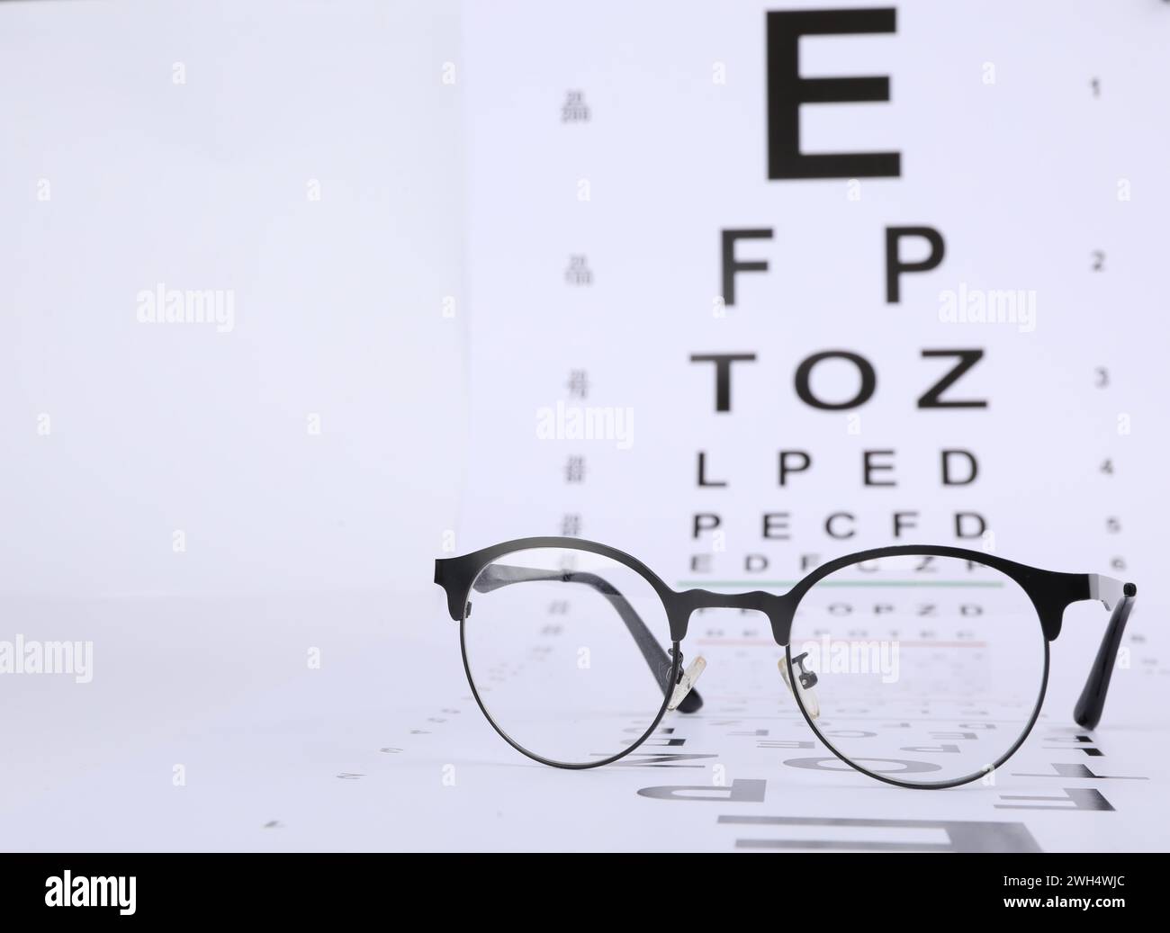 Vision test chart and glasses on white background, closeup. Space for ...