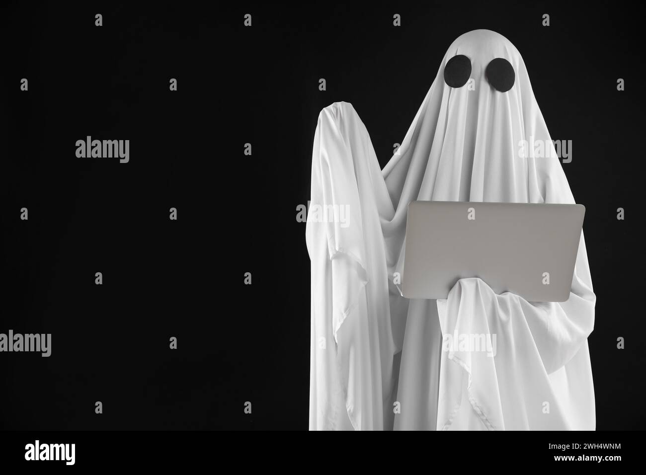 Creepy ghost. Person in white sheet with laptop on black background ...
