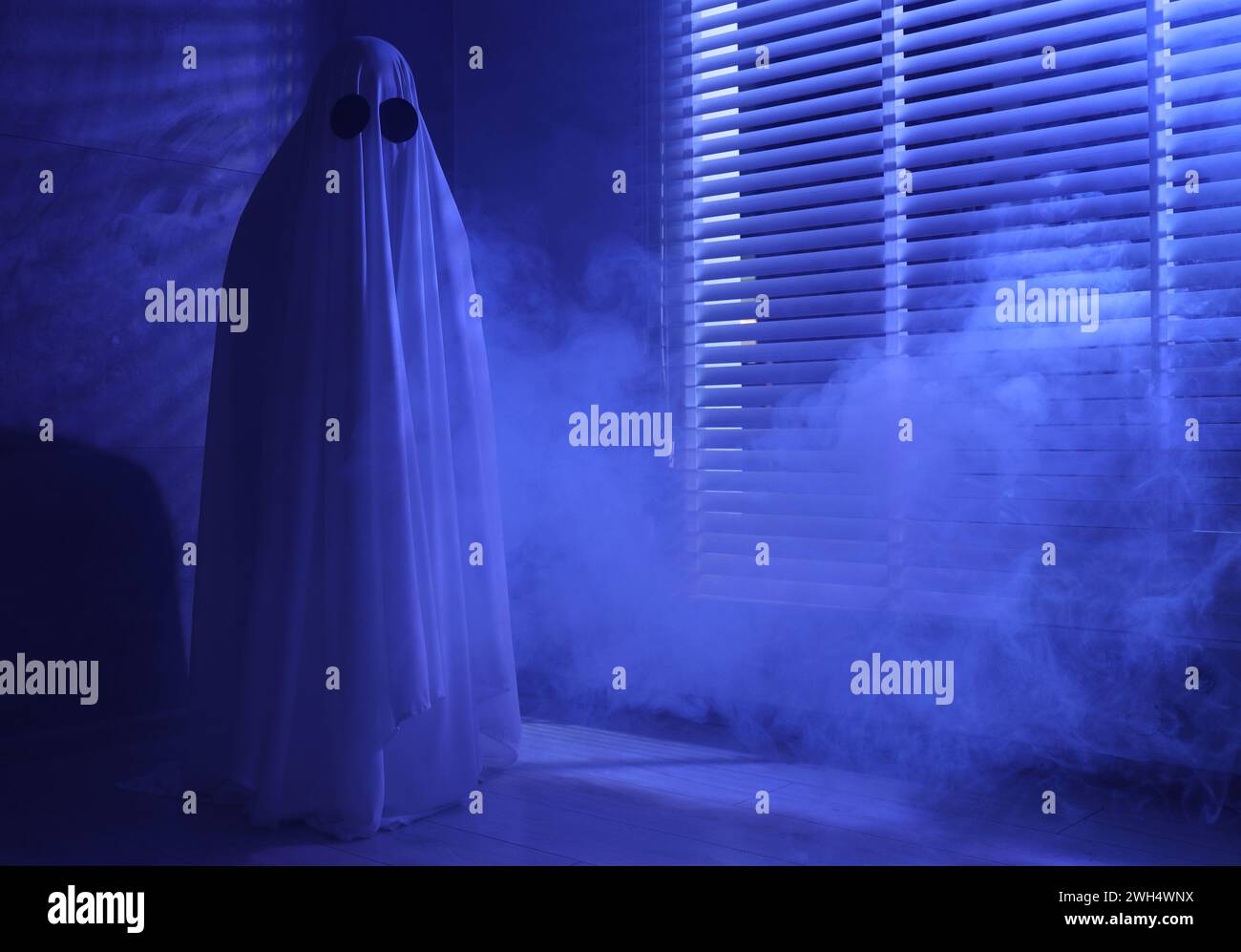 Creepy ghost. Woman covered with sheet near window in blue light Stock ...