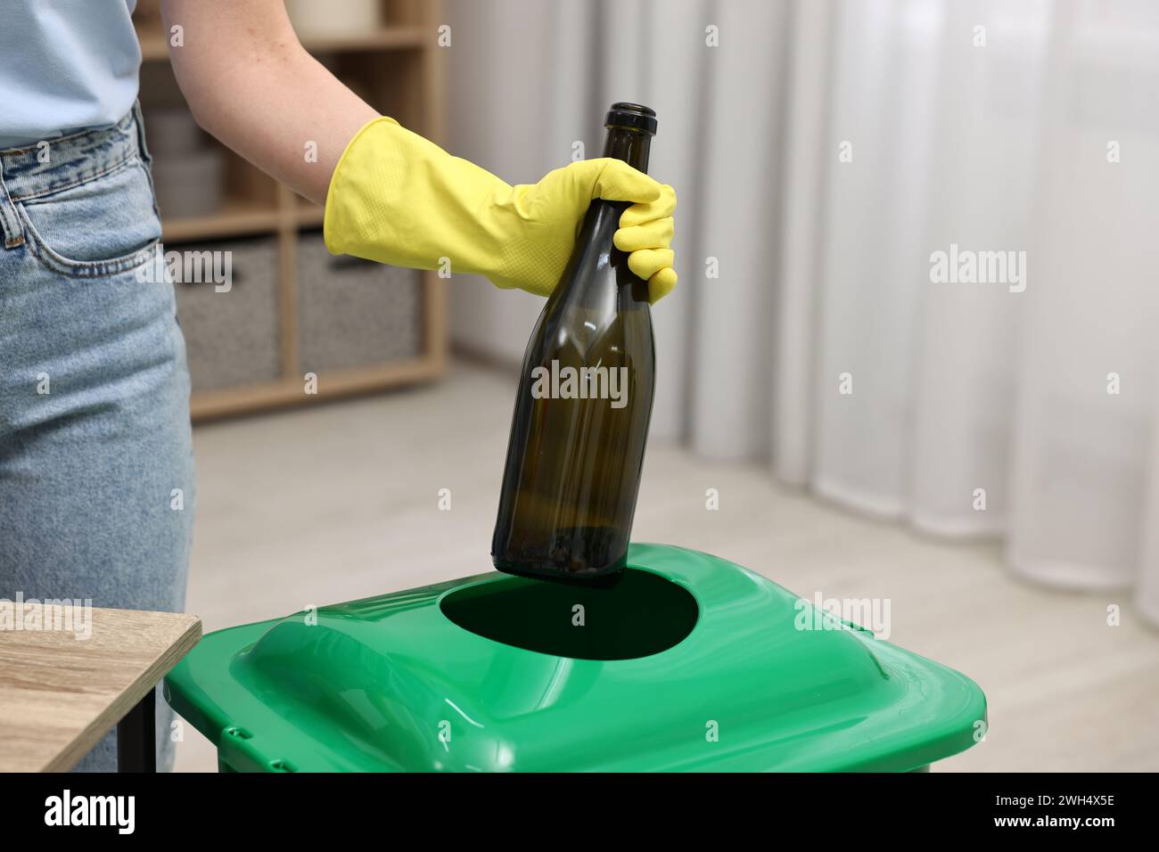 Garbage sorting. Woman throwing glass bottle into trash bin in room, closeup Stock Photo - Alamy