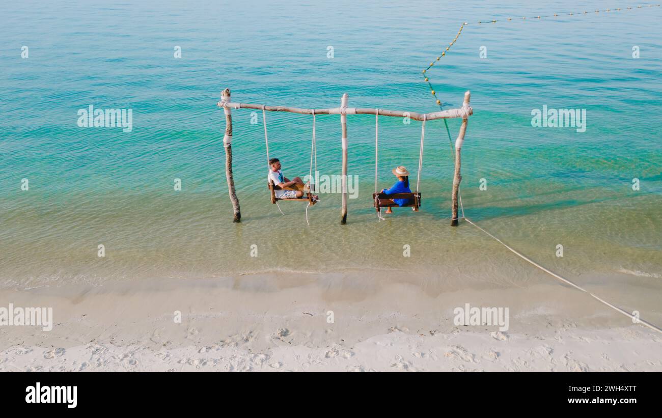 a couple of men and a woman on a swing at the beach of Koh Muk, a ...